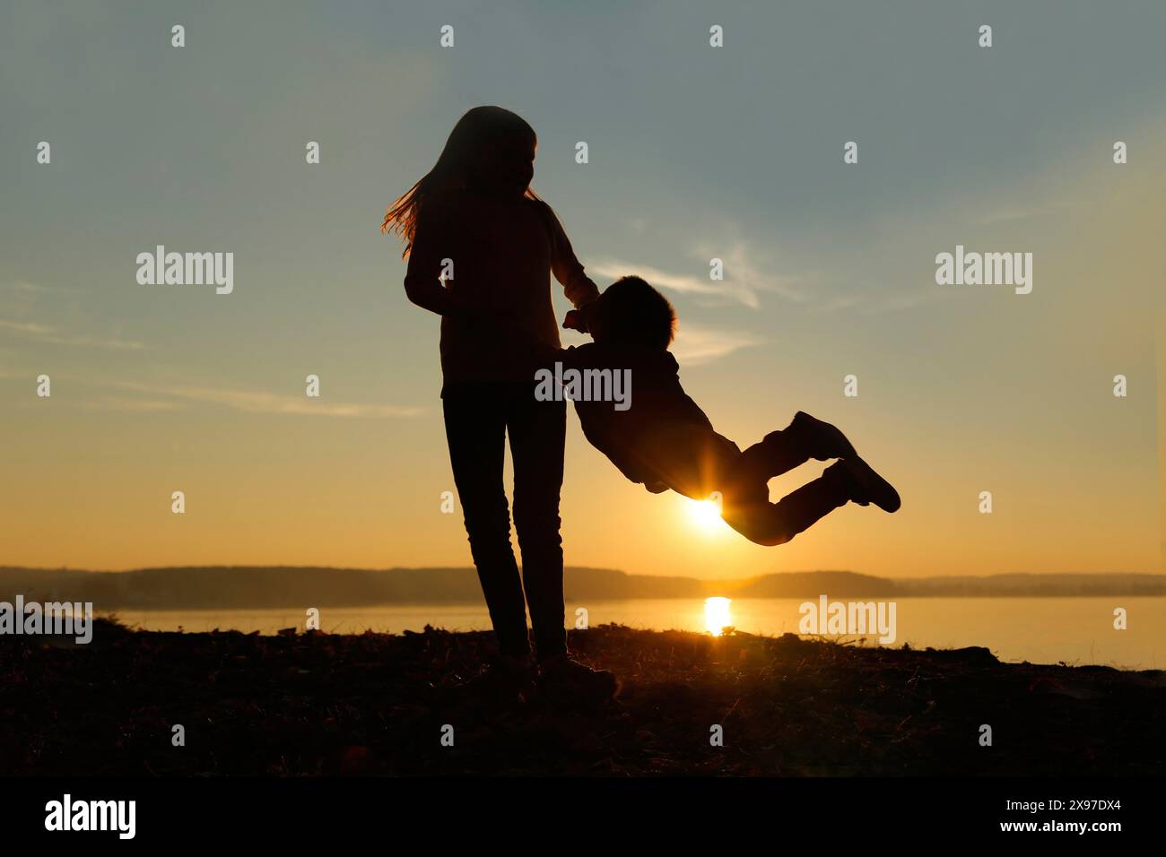 Two children playing near water during a sunset, captured in a ...