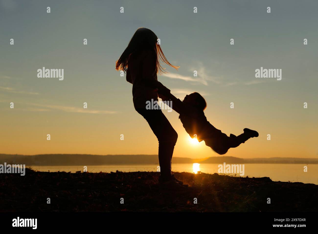 Silhouette of a parent spinning a child at sunset near a lake Stock ...