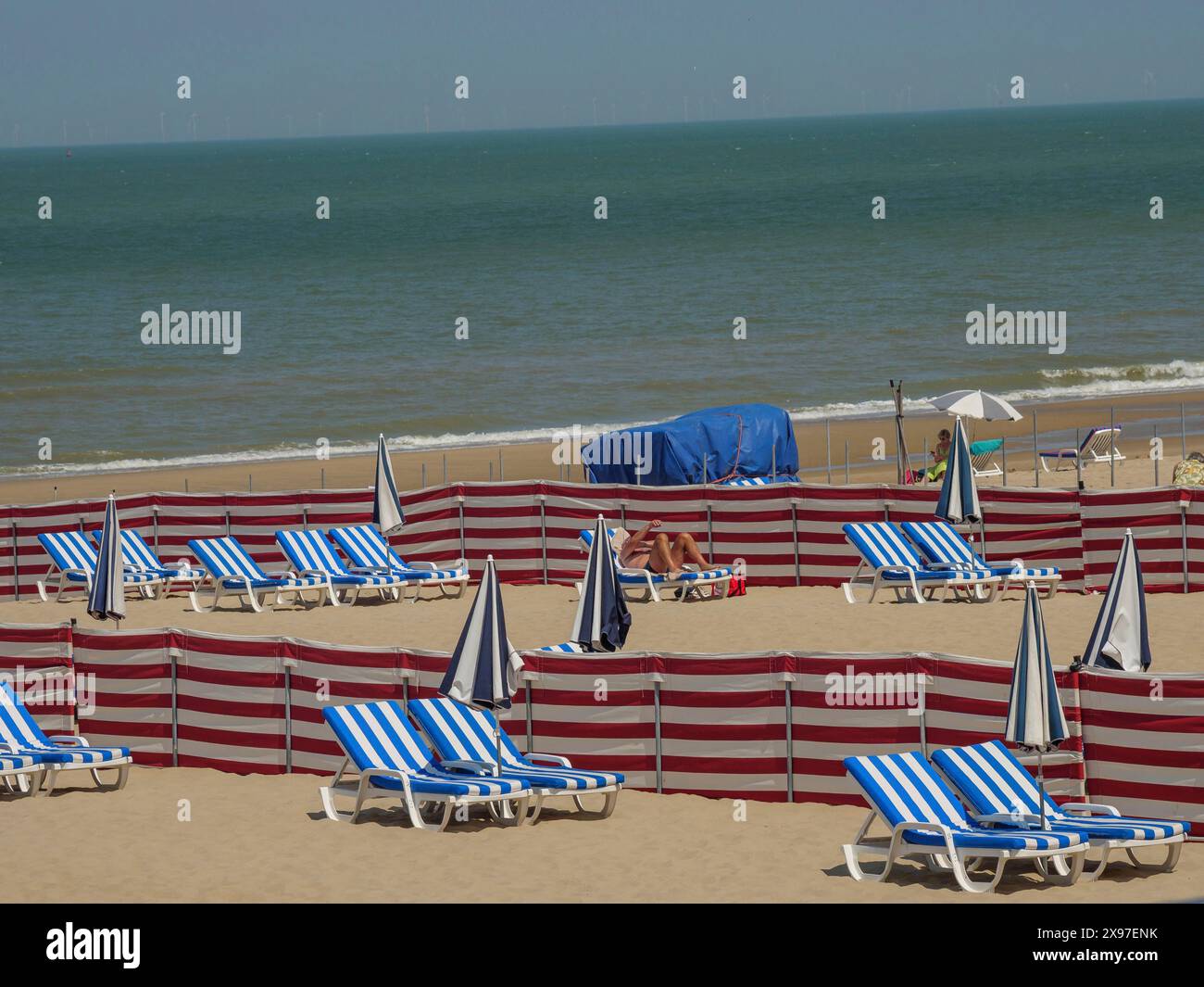 Beach with several blue and white striped sun loungers and parasols ...