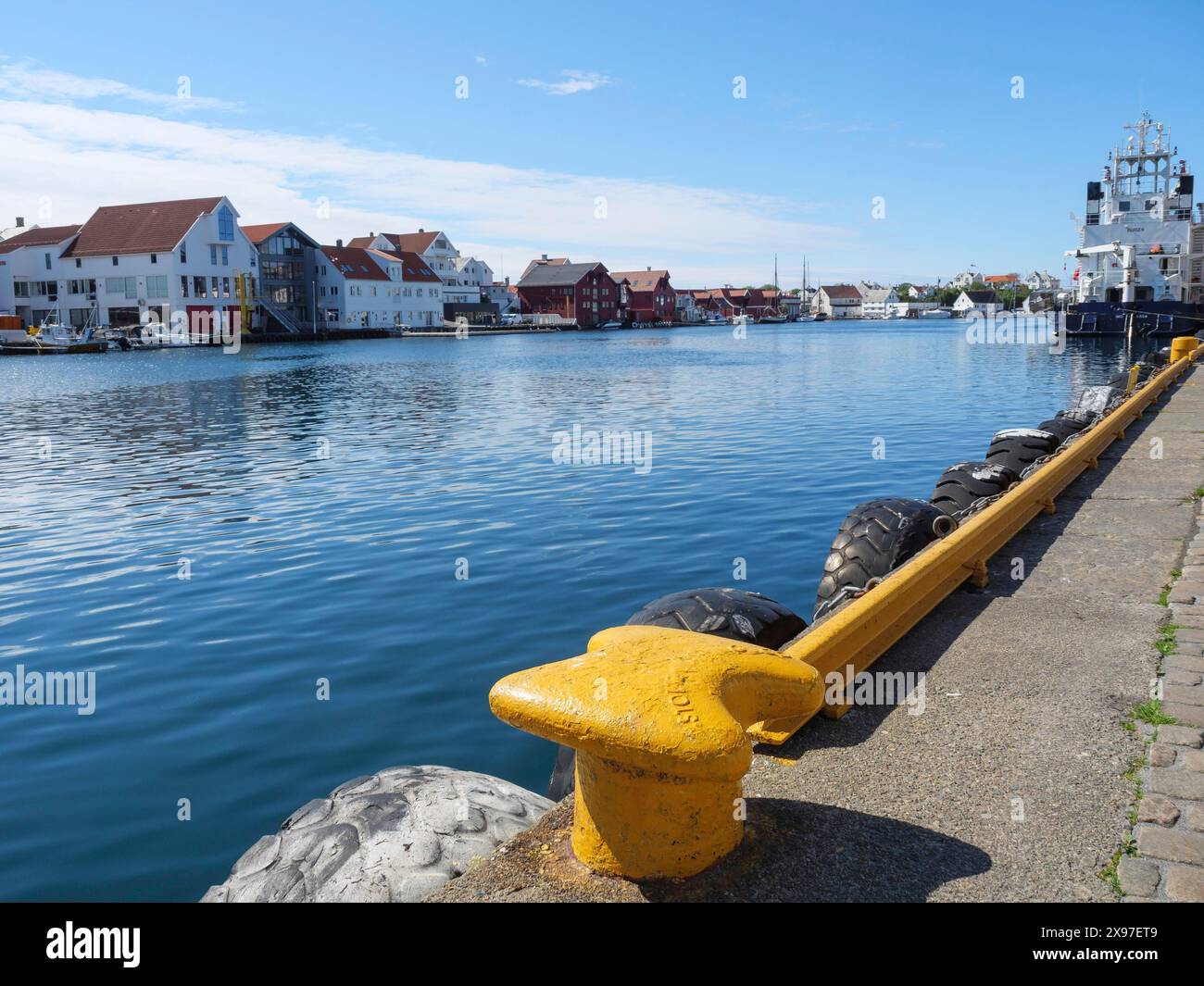 Waterfront with a yellow bollard and tyre protection, water and city in ...