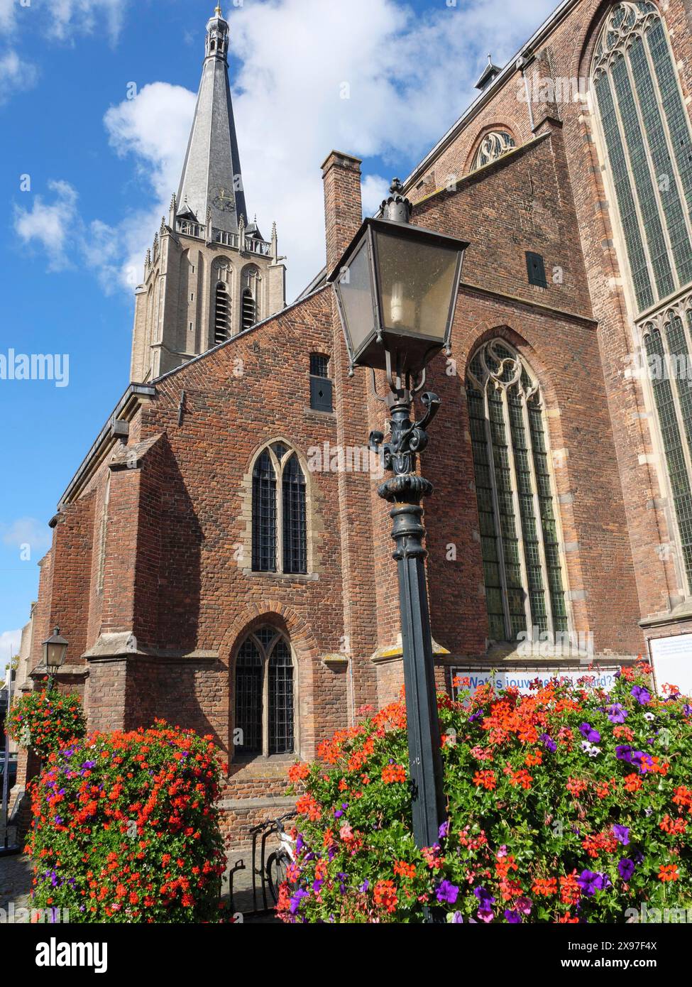 Historic red brick gothic church with high steeple, a large flower bed ...