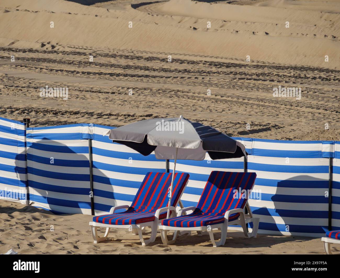 Blue and white striped deckchairs next to a parasol on the beach ...