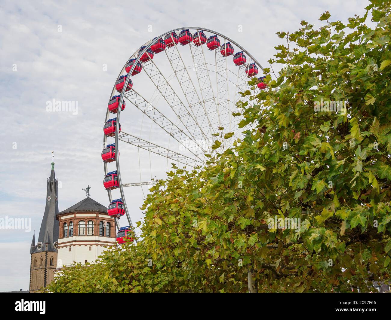 Red Ferris wheel next to a church tower and a historic building behind ...