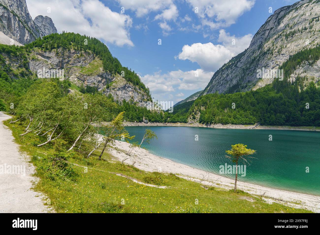 Path on the shore of a lake between mountains under a cloudy sky ...