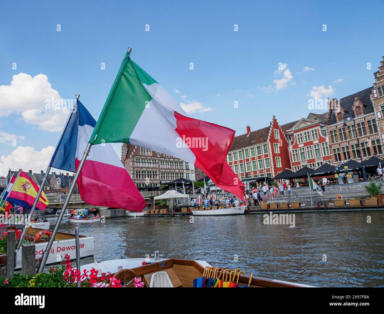 Flags waving on the banks of a river, people and historic buildings in ...
