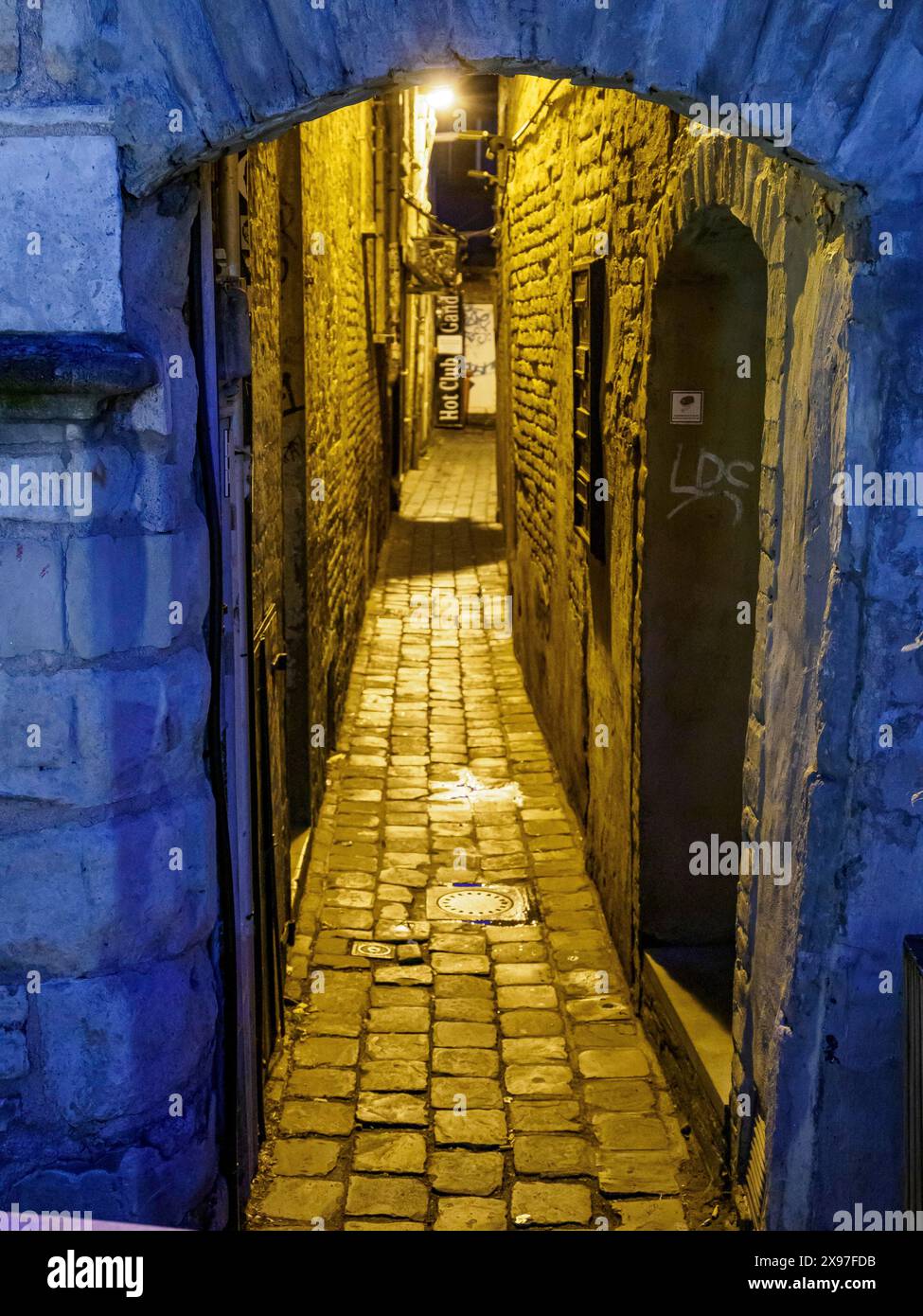 Narrow, cobbled alley between historic buildings, illuminated in warm ...