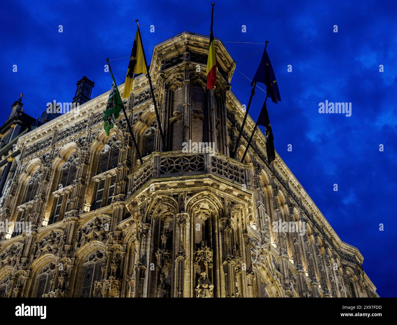 Historic gothic facade of a building at night with several flags and ...