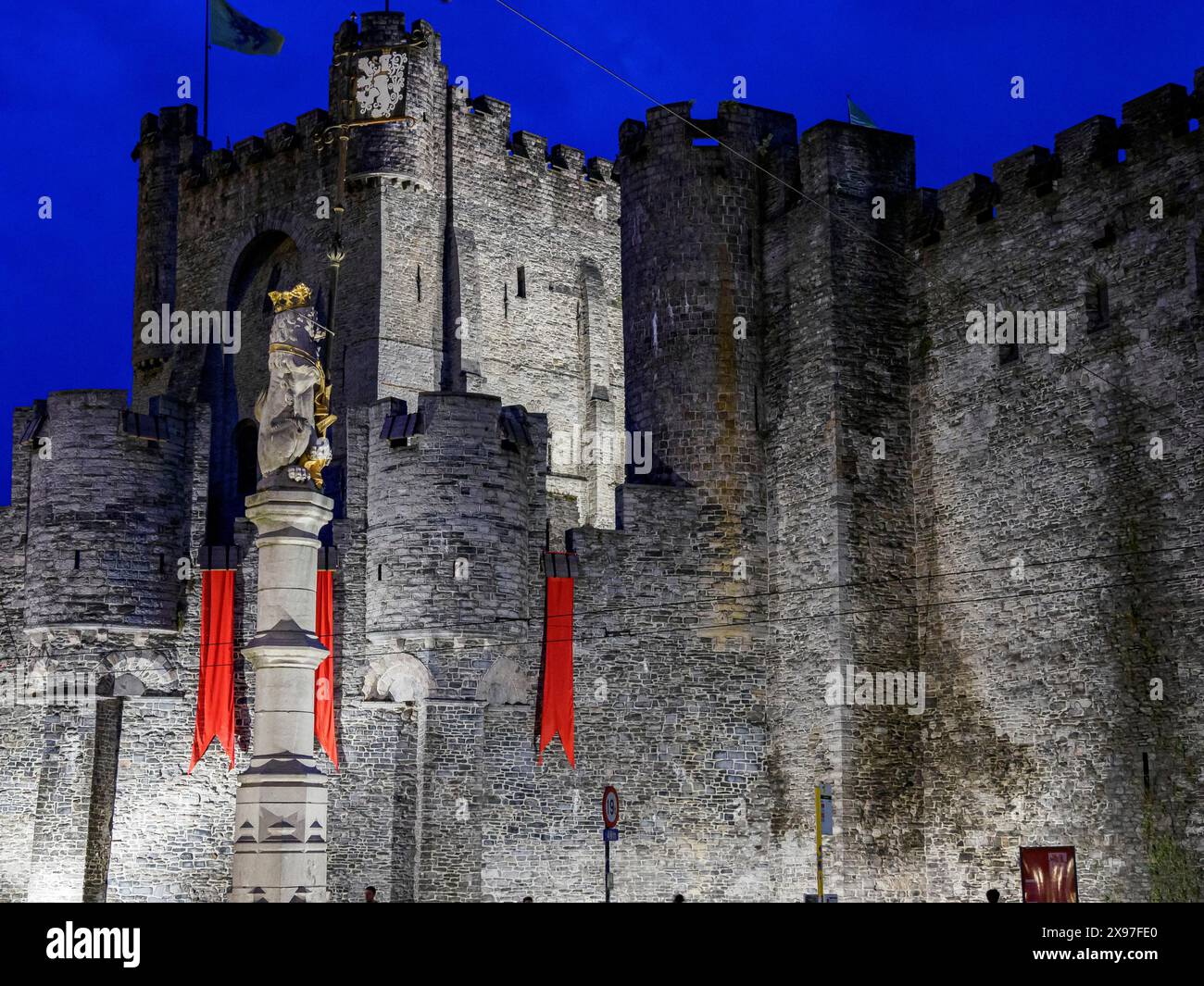 Medieval castle with massive stone walls, a statue and red flags ...