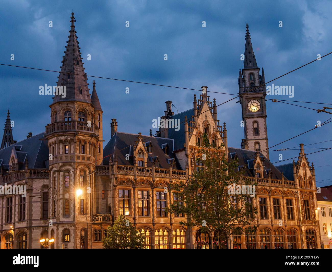 Historic gothic building with clock tower and illuminated street lamps ...