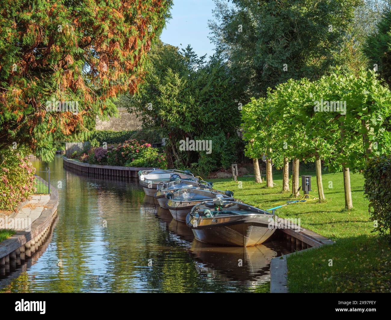 Boats are docked along a quiet canal, surrounded by trees and lush greenery, boats on small ...