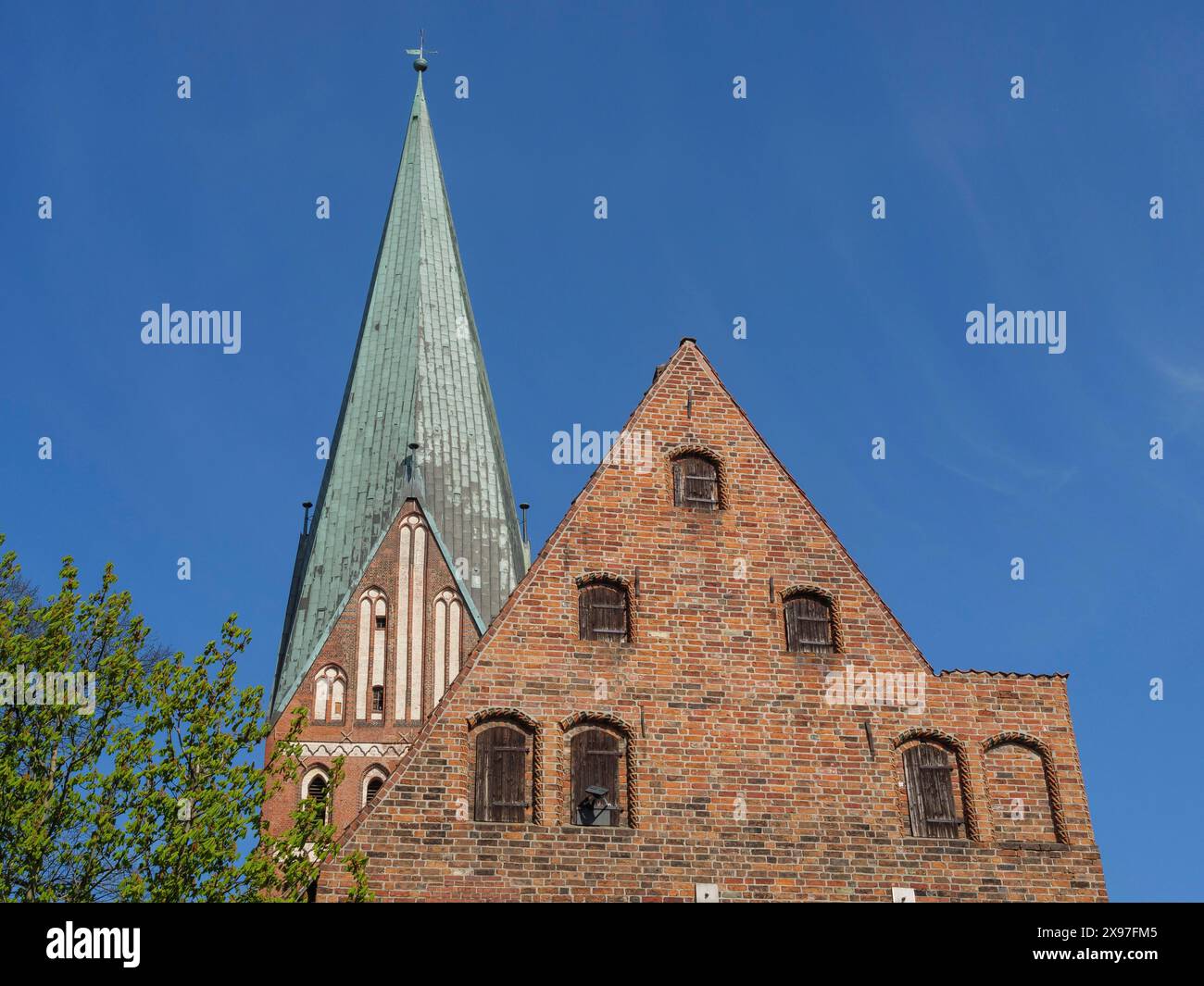 Church tower and gable of a brick gothic church with trees and blue sky ...
