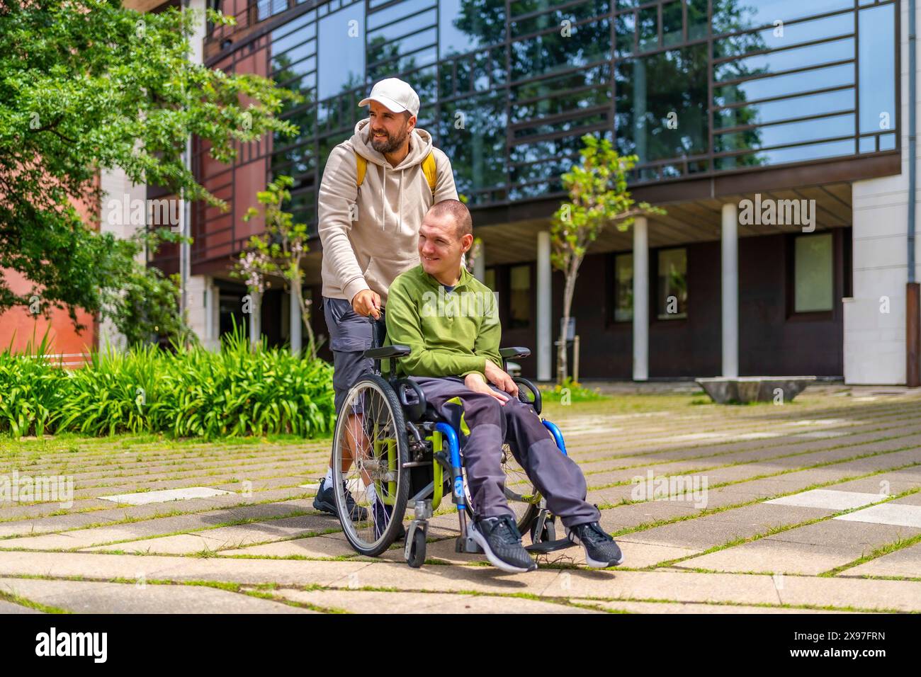 University student pushing the wheelchair of a disabled friend outdoors ...