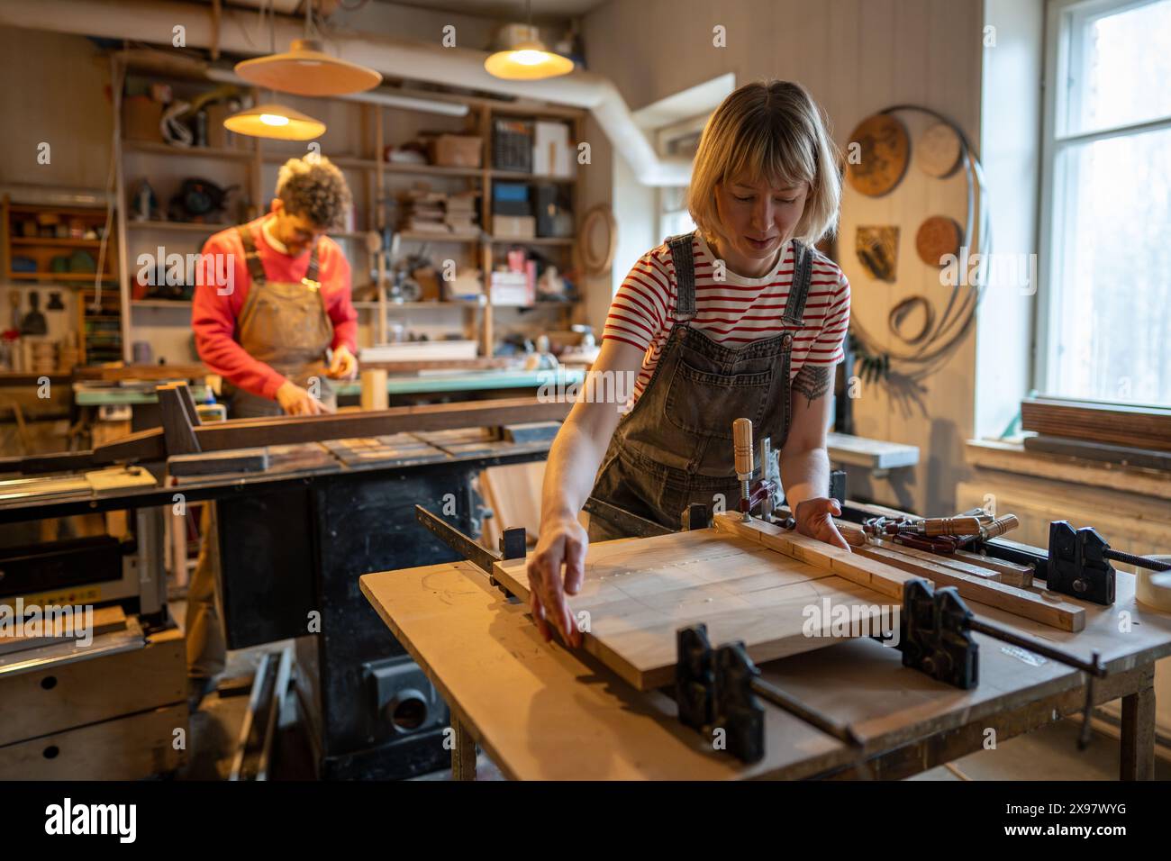Concentrated female carpenter working on gluing wooden planks together ...