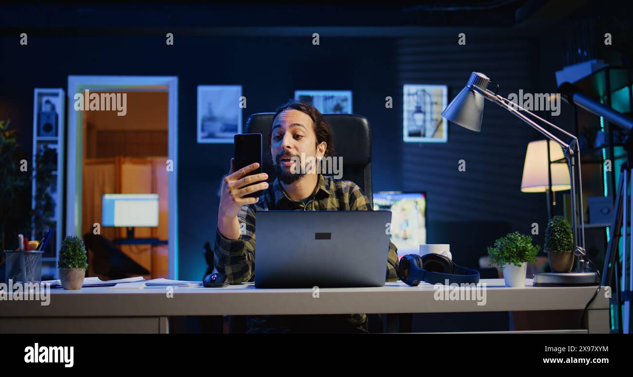 Man receiving phone call from friend while working from home on laptop in personal office ...