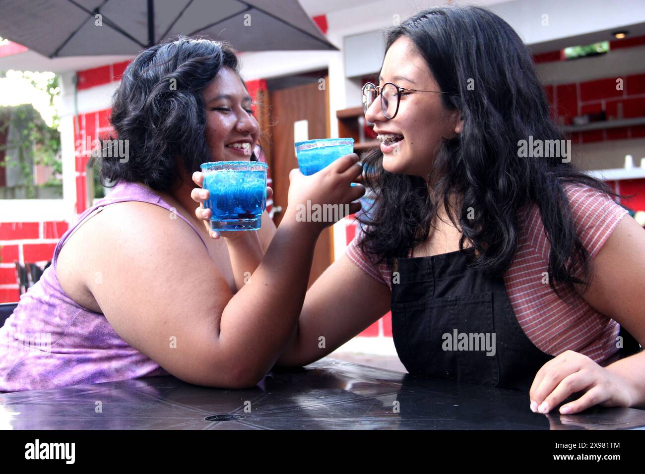 Two young brunette Latin women of 20 years old drink frosty blue ...