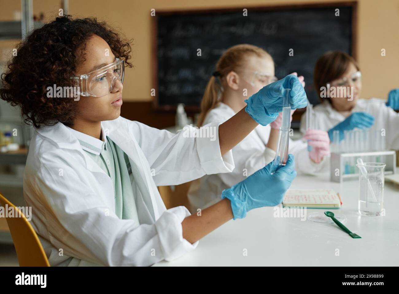 African American schoolboy wearing lab coat sitting at table in ...