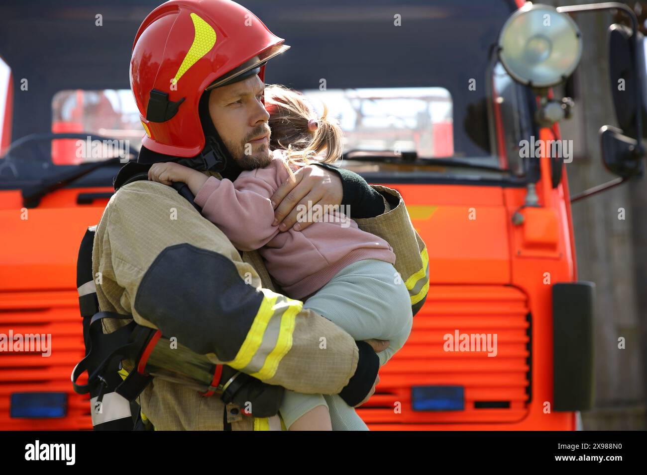 Firefighter in uniform holding rescued little girl near fire truck ...