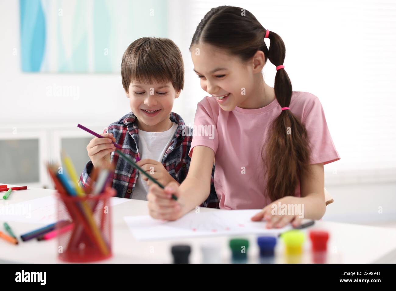 Happy brother and sister drawing at white table in room Stock Photo - Alamy