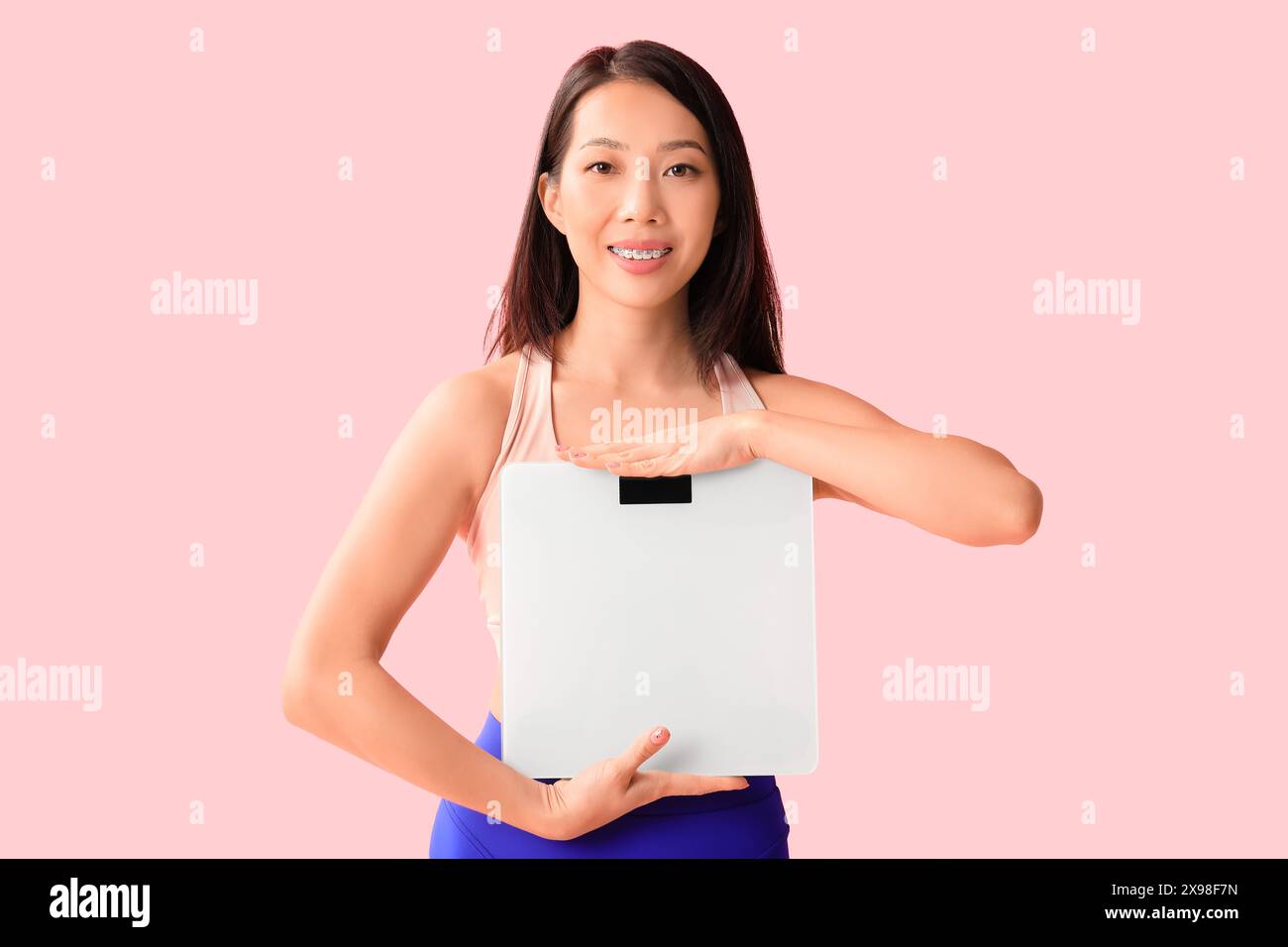 Beautiful young Asian woman with scales on pink background. Weight loss ...