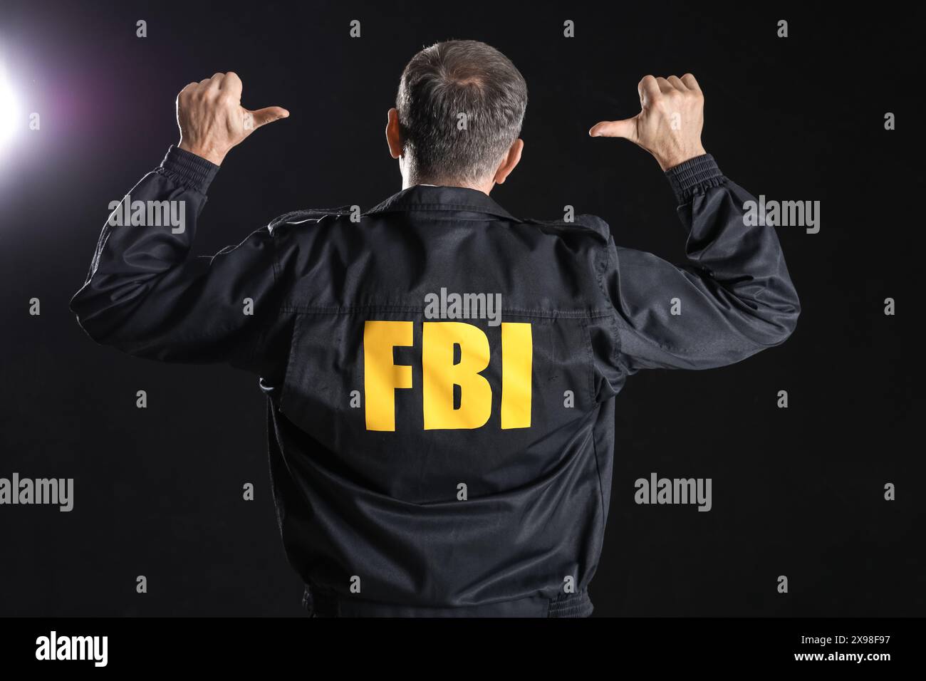 Mature FBI agent pointing at himself on black background, back view ...