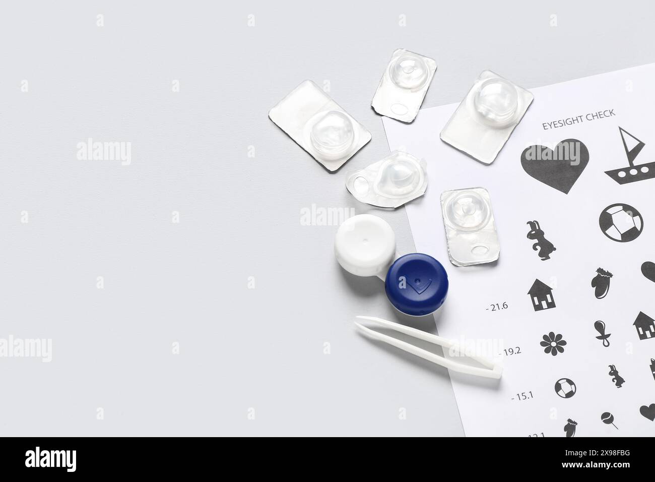 Eye test chart with tweezers, container and contact lenses on white ...