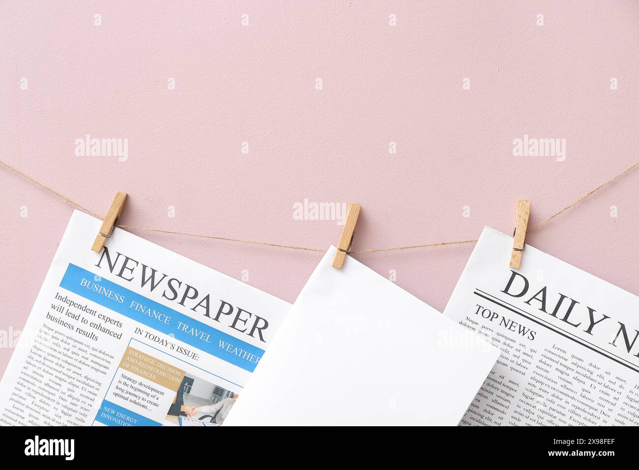 Newspapers and blank sheet of paper hanging on rope against pink ...