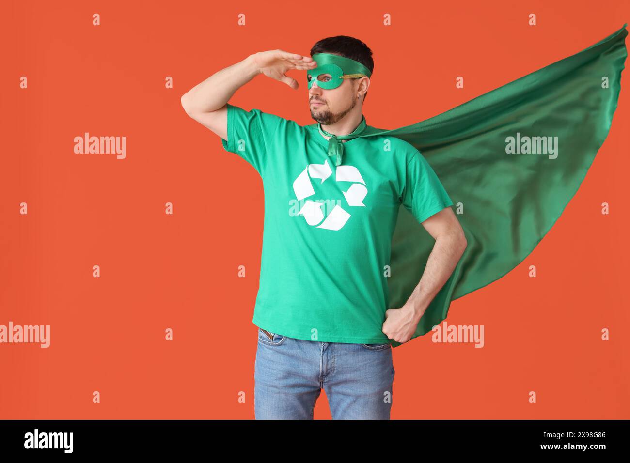 Young man dressed as eco superhero looking at something on orange ...