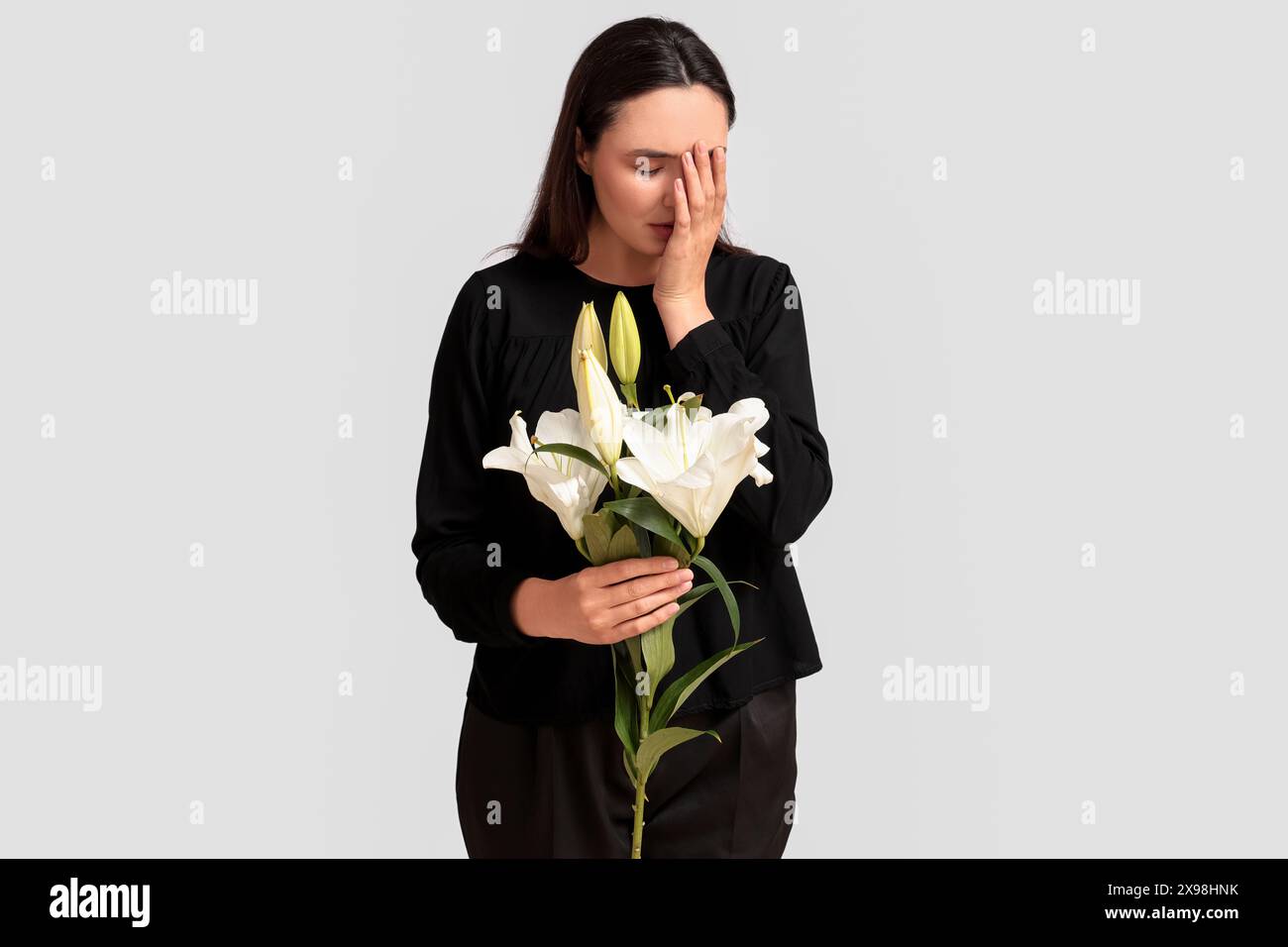 Young crying woman with funeral lily flowers on white background Stock ...