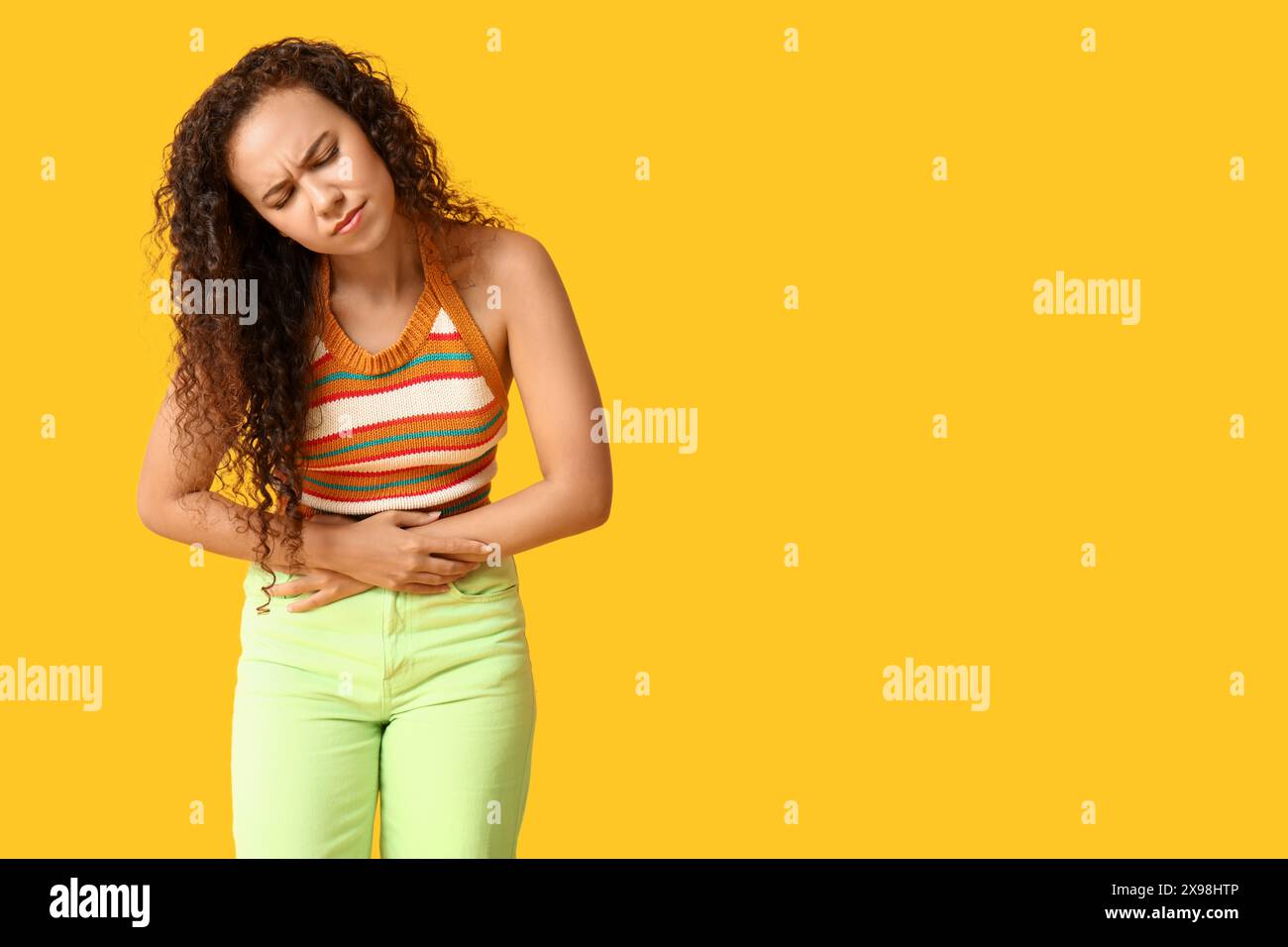 Young African-American woman with stomach ache on yellow background ...