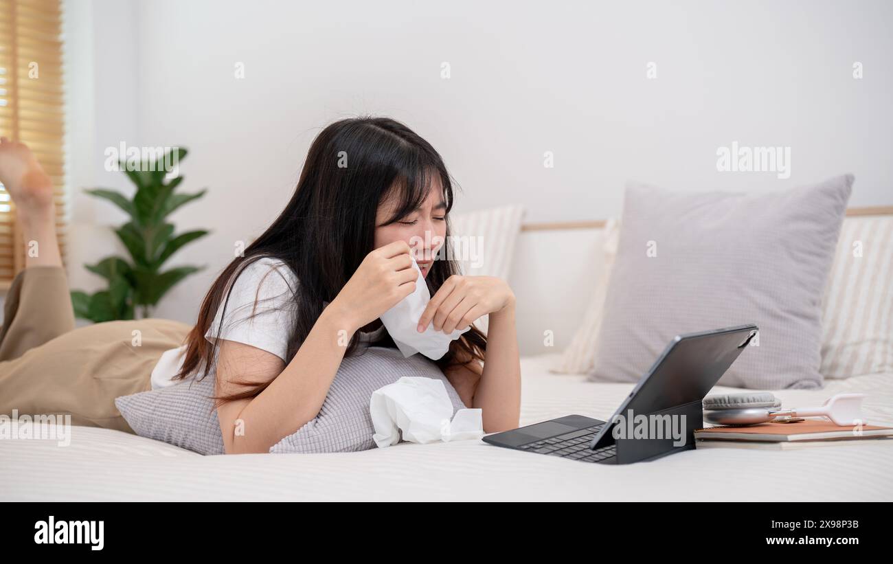 A beautiful young Asian woman is lying on the bed, crying, and wiping ...