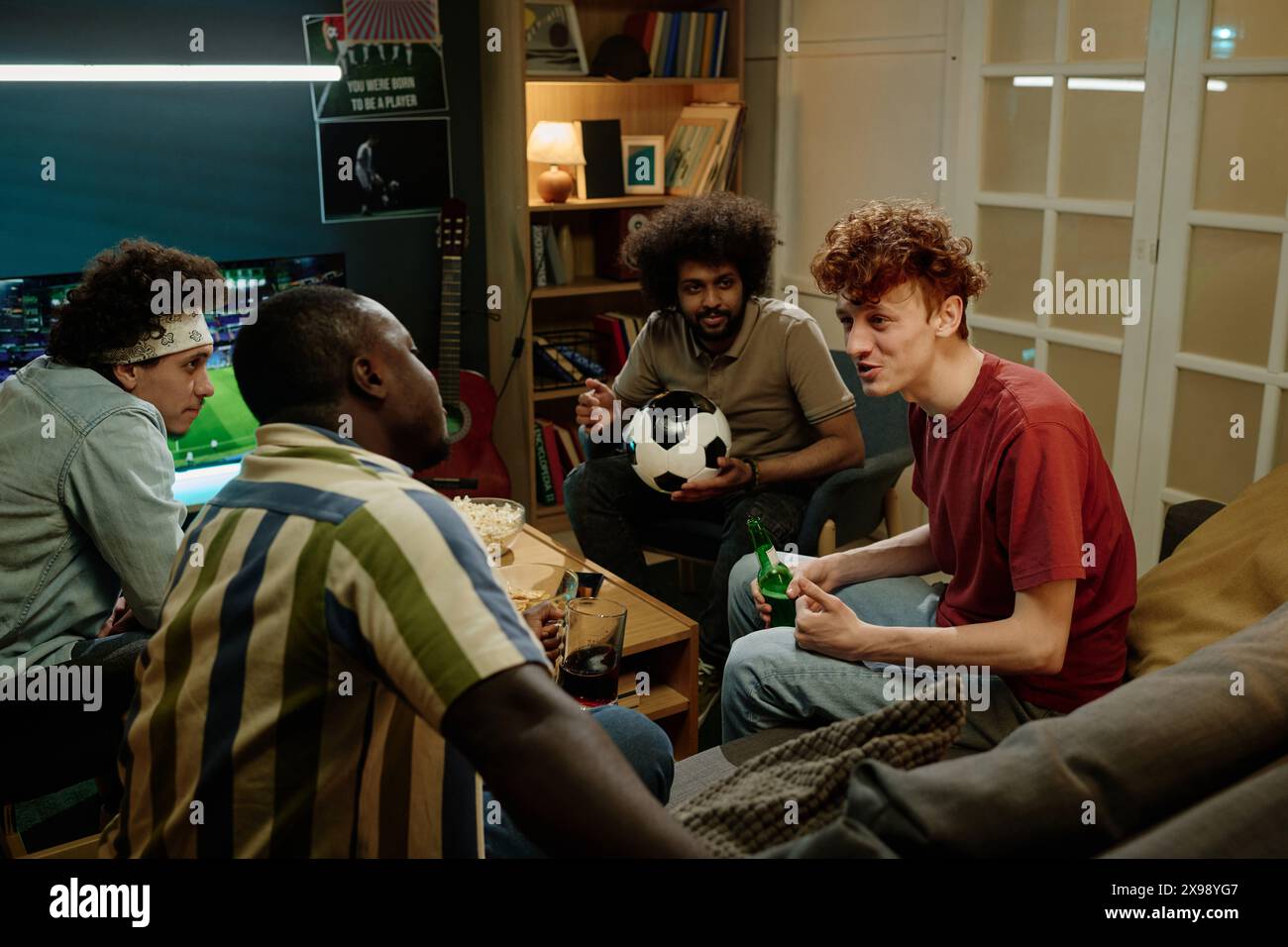 Multi-ethnic group of four young men sitting in living room discussing ...
