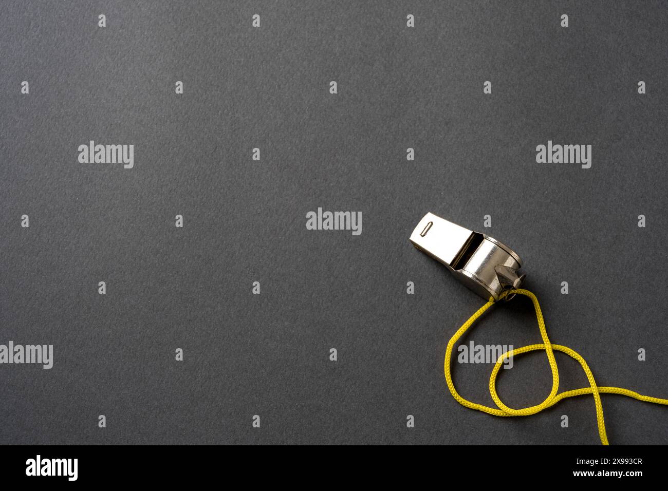 Top view of metal whistle with yellow string on dark gray background ...