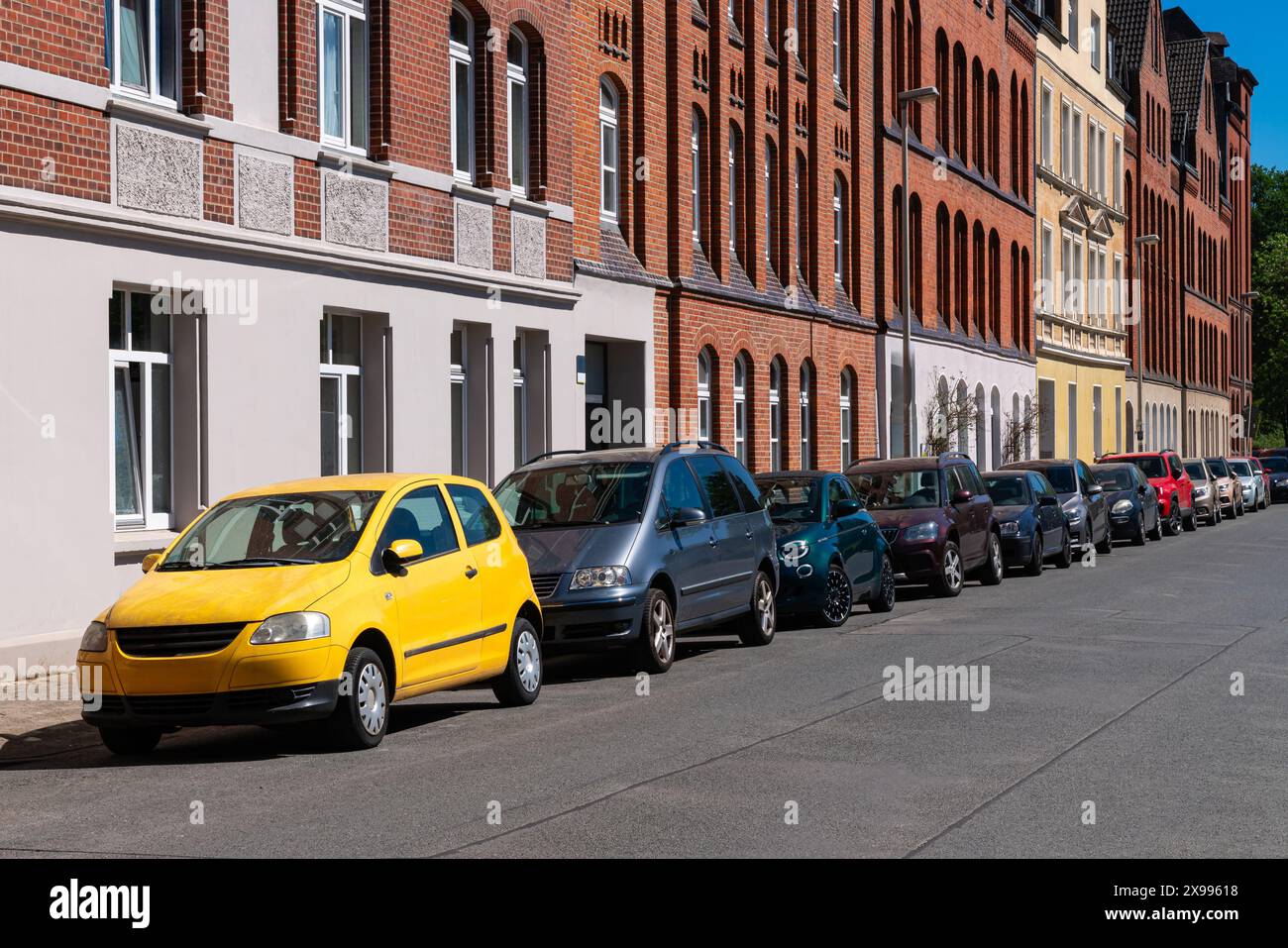 A row of cars standing on the side of the road with a bright yellow car ...