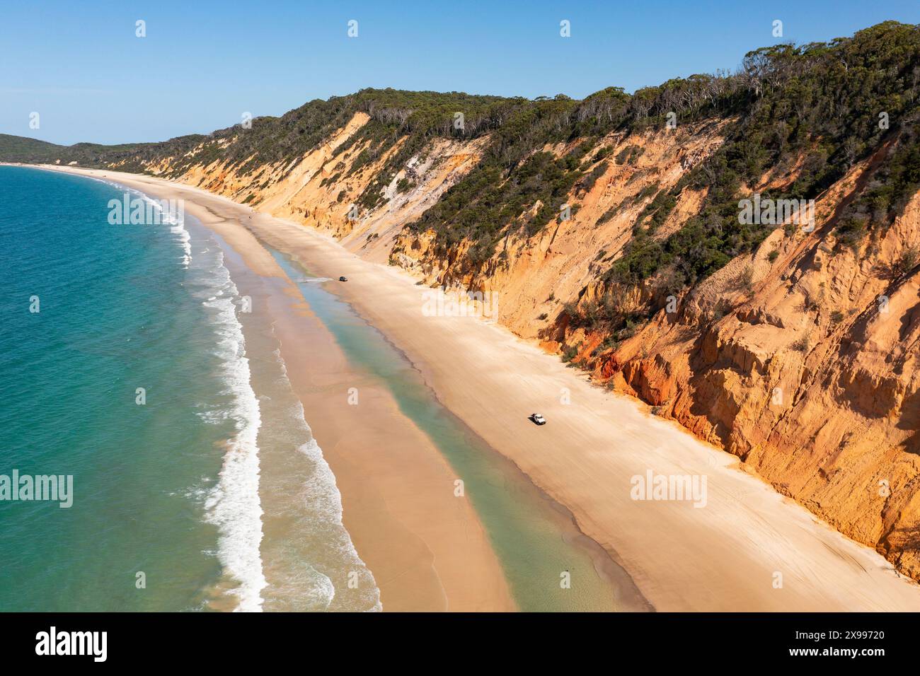 Aerial view a narrow beach below tall colourful sea cliffs at Rainbow ...