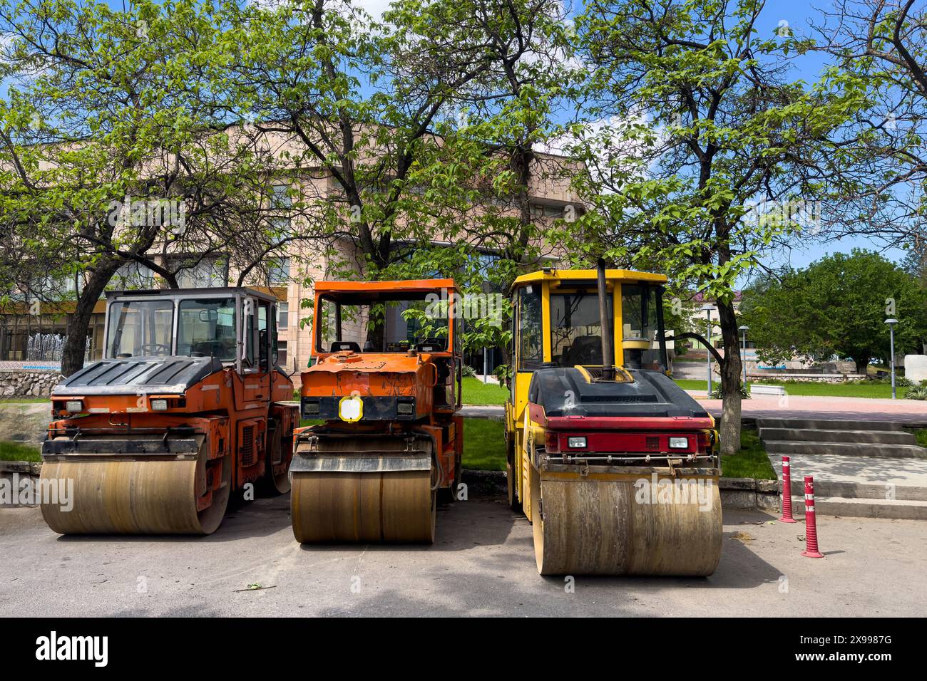Three old asphalt rollers stand on the side of the road. Building in ...