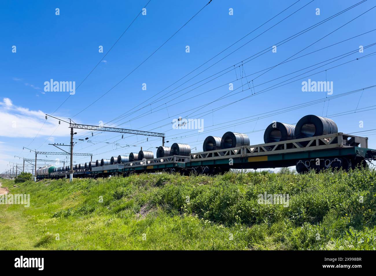 Train platforms loaded with sheet metal in large rolls under a blue sky ...