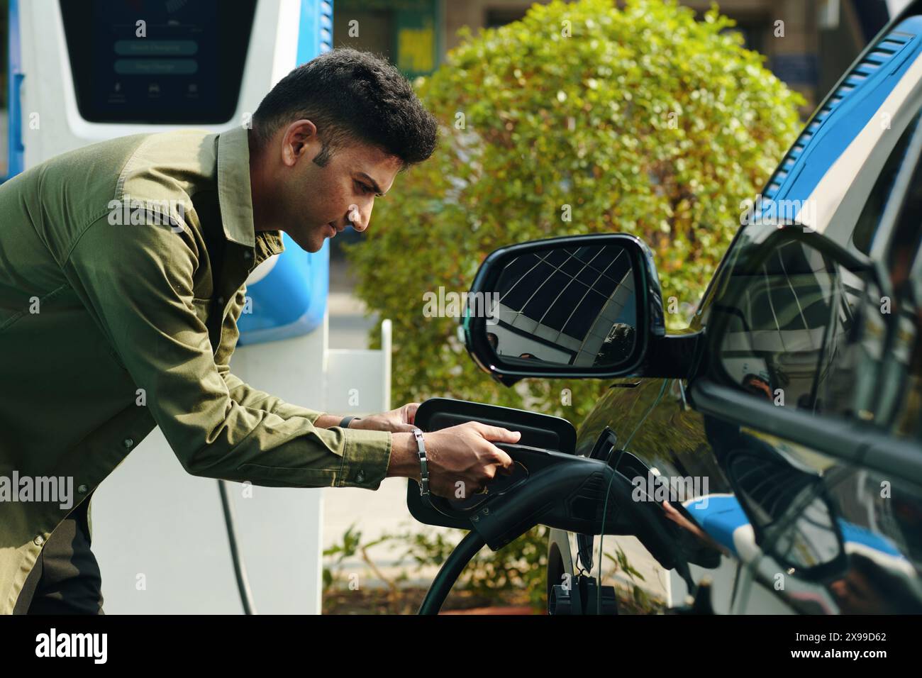 Electric car owner charging his vehicle at station Stock Photo - Alamy