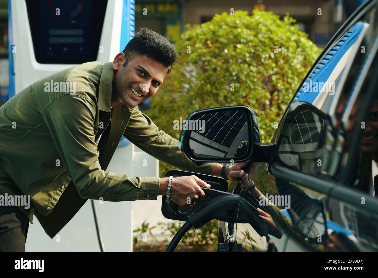 Smiling Indian man charging electric vehicle at station Stock Photo - Alamy