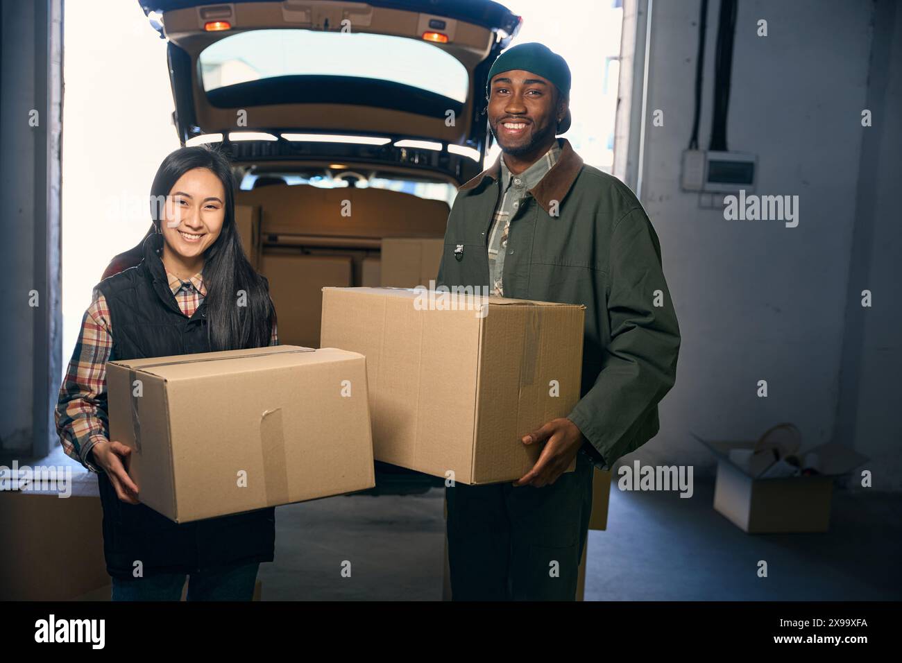 Smiling man and woman are unloading things from the trunk of a car ...