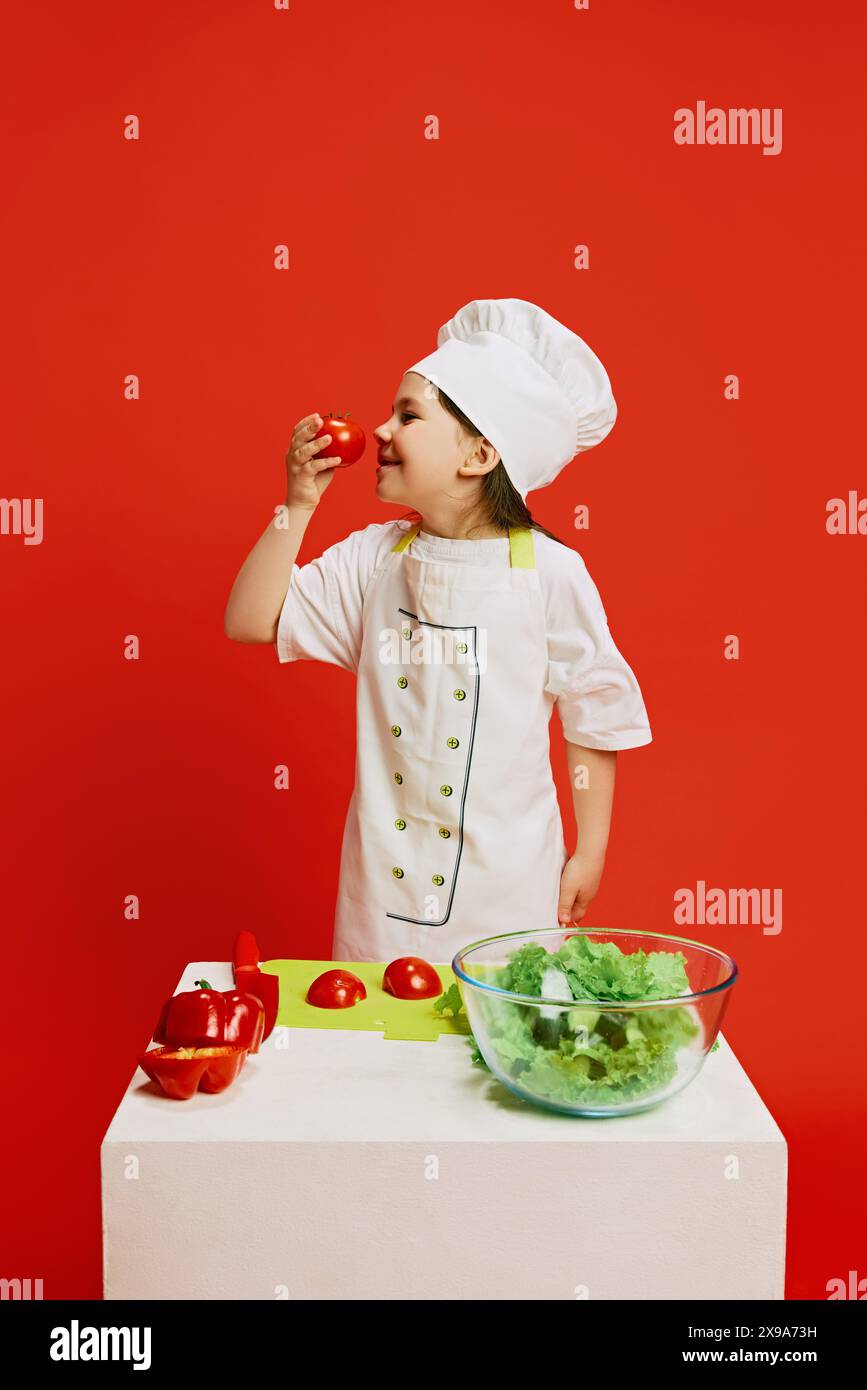 Cooking career. Child in chef's outfit, preparing salad, smiling by ...
