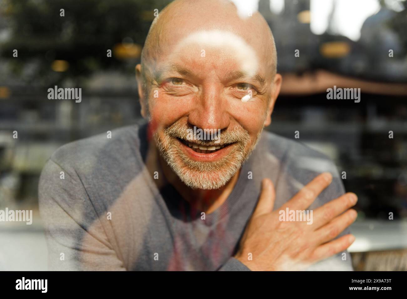 Happy senior man with a beard smiling through a glass window ...