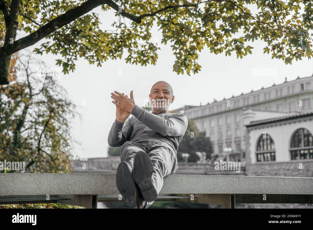 Elderly man clapping hands joyfully while sitting on a bench, park ...