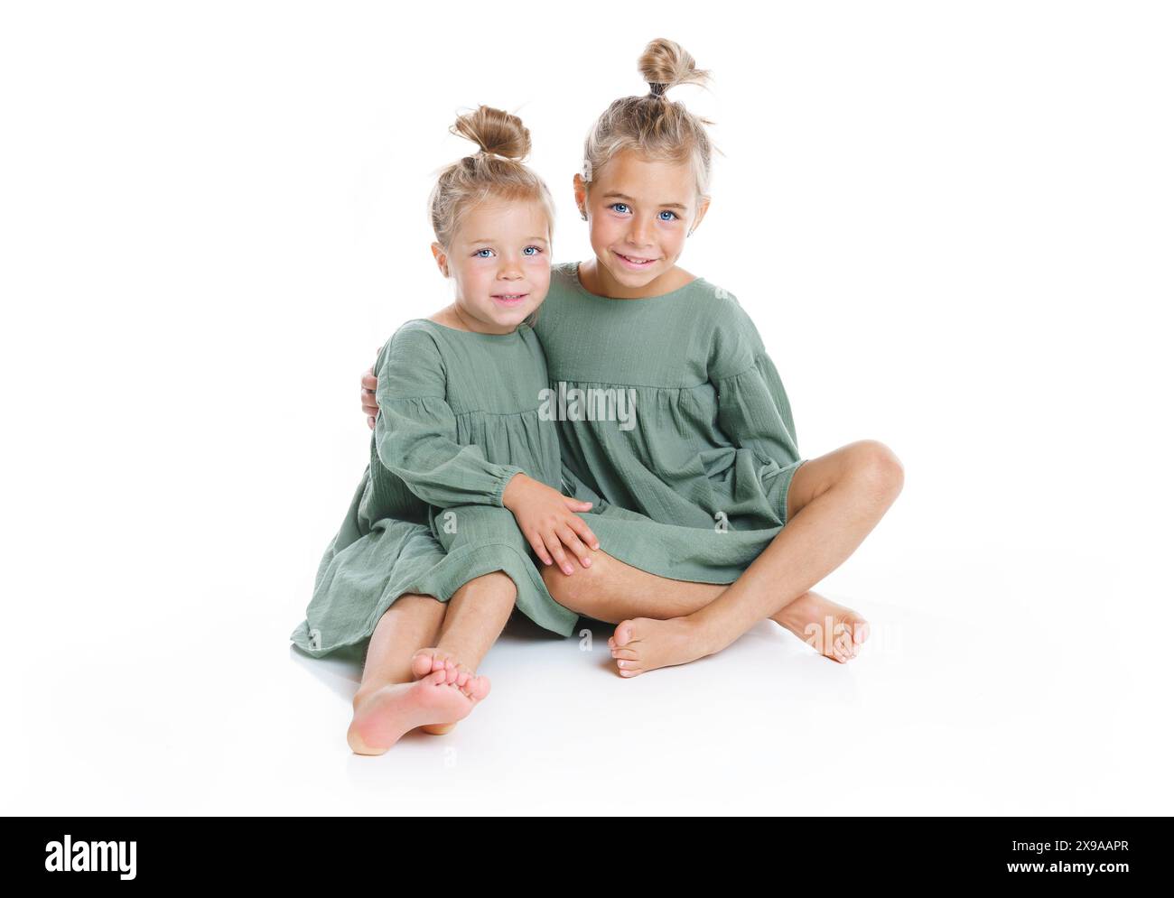 Two cute little sisters on the floor arm in arm cuddling each other in ...