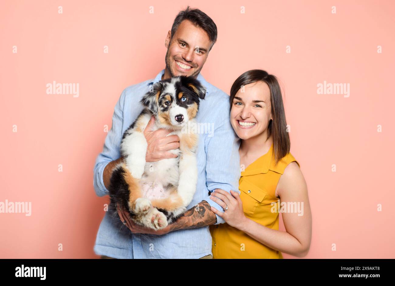 Handsome couple with her Australian Berger puppy on studio pink color ...