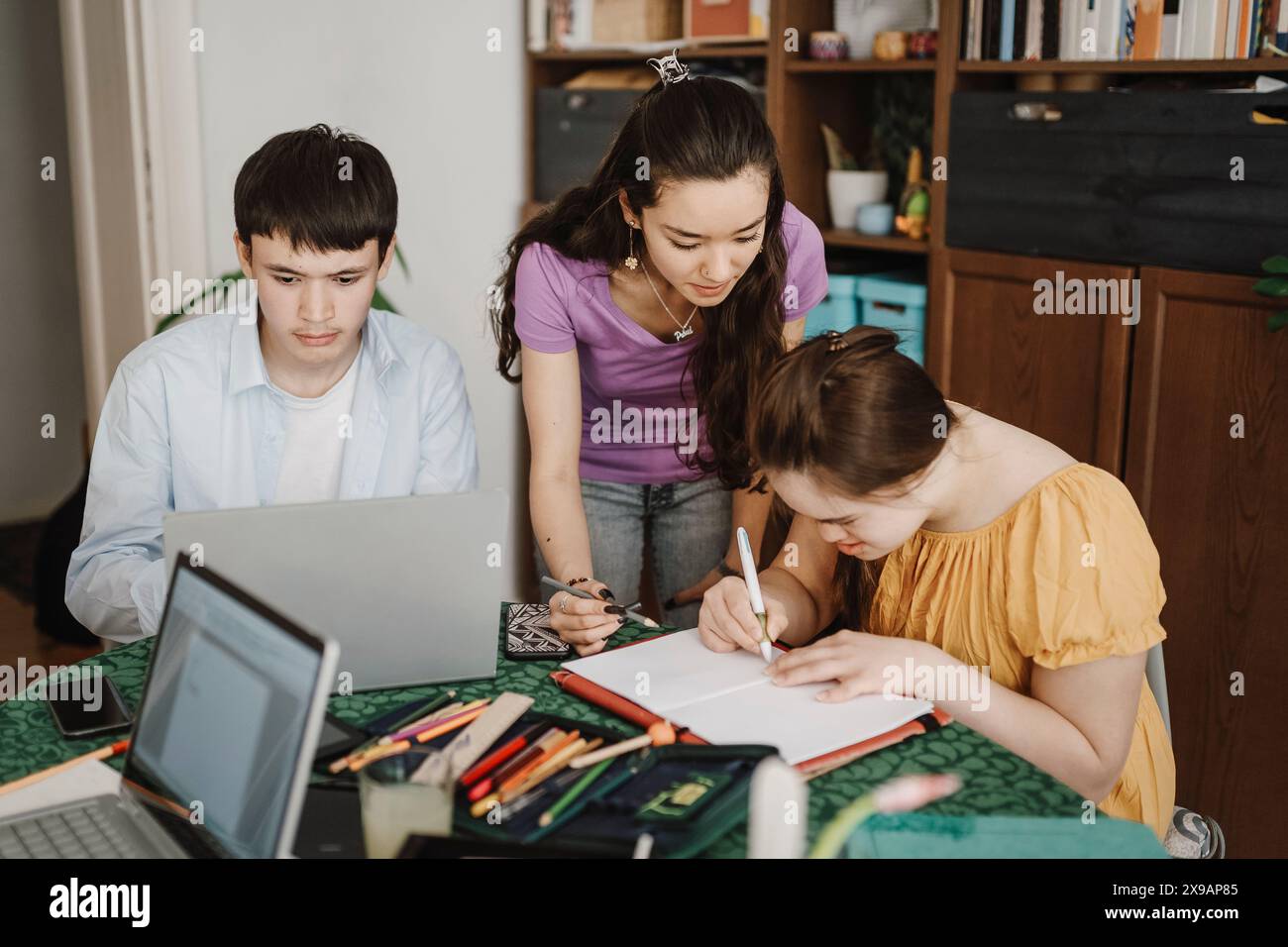 Siblings assisting down syndrome sister while doing homework at home ...