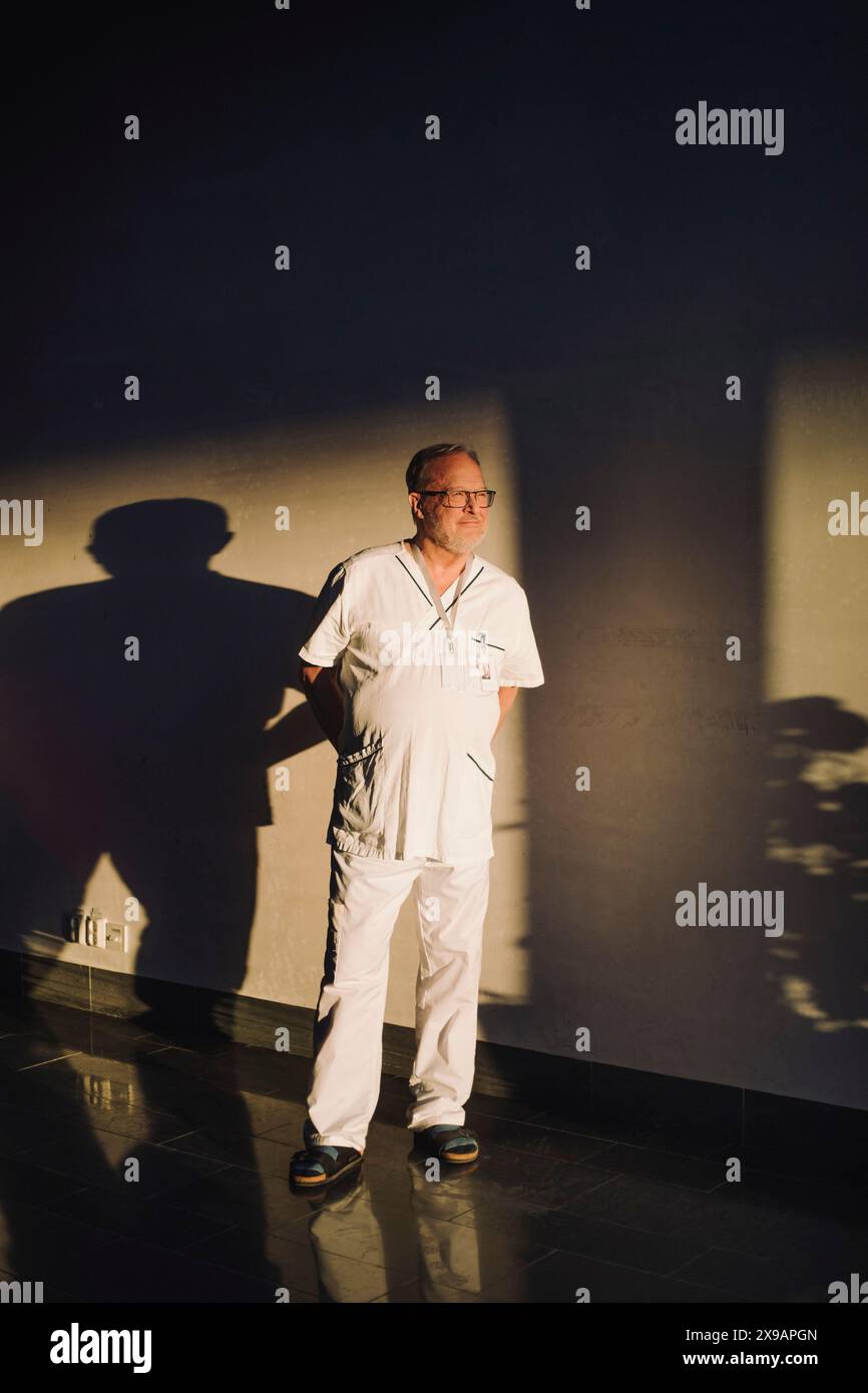 Full length shot of senior male doctor standing in front of wall at ...