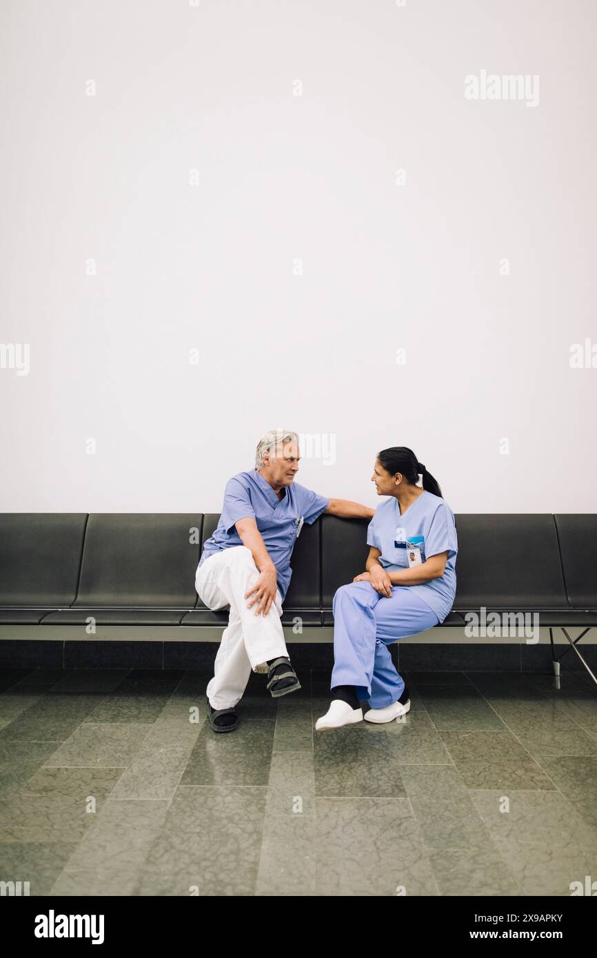 Male and female doctors discussing while sitting on bench in hospital ...