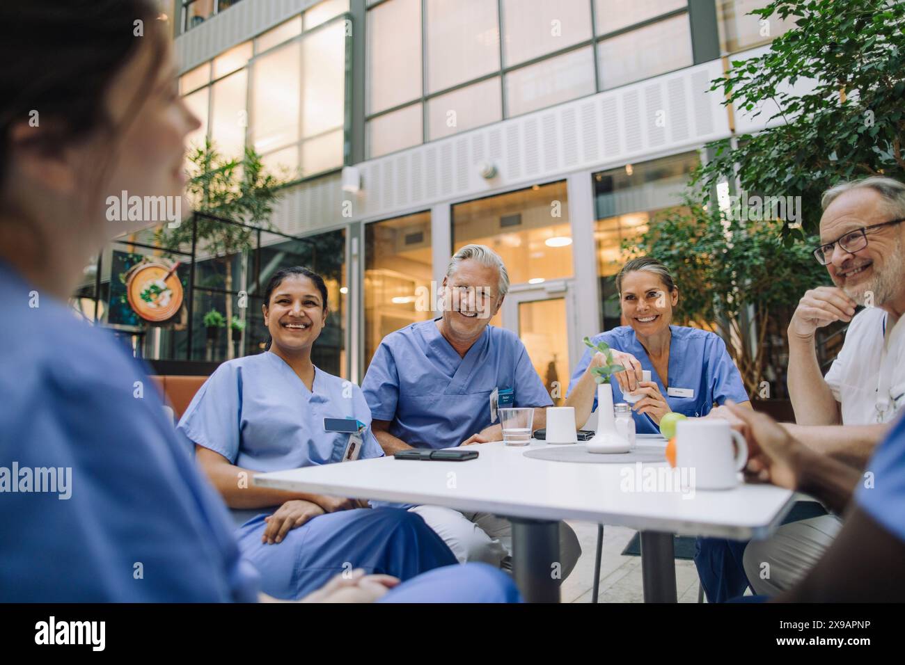Happy male and female doctors sitting at table in cafeteria of hospital ...