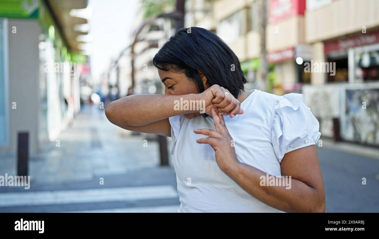 A middle-aged hispanic woman sneezing into her elbow on a busy urban ...