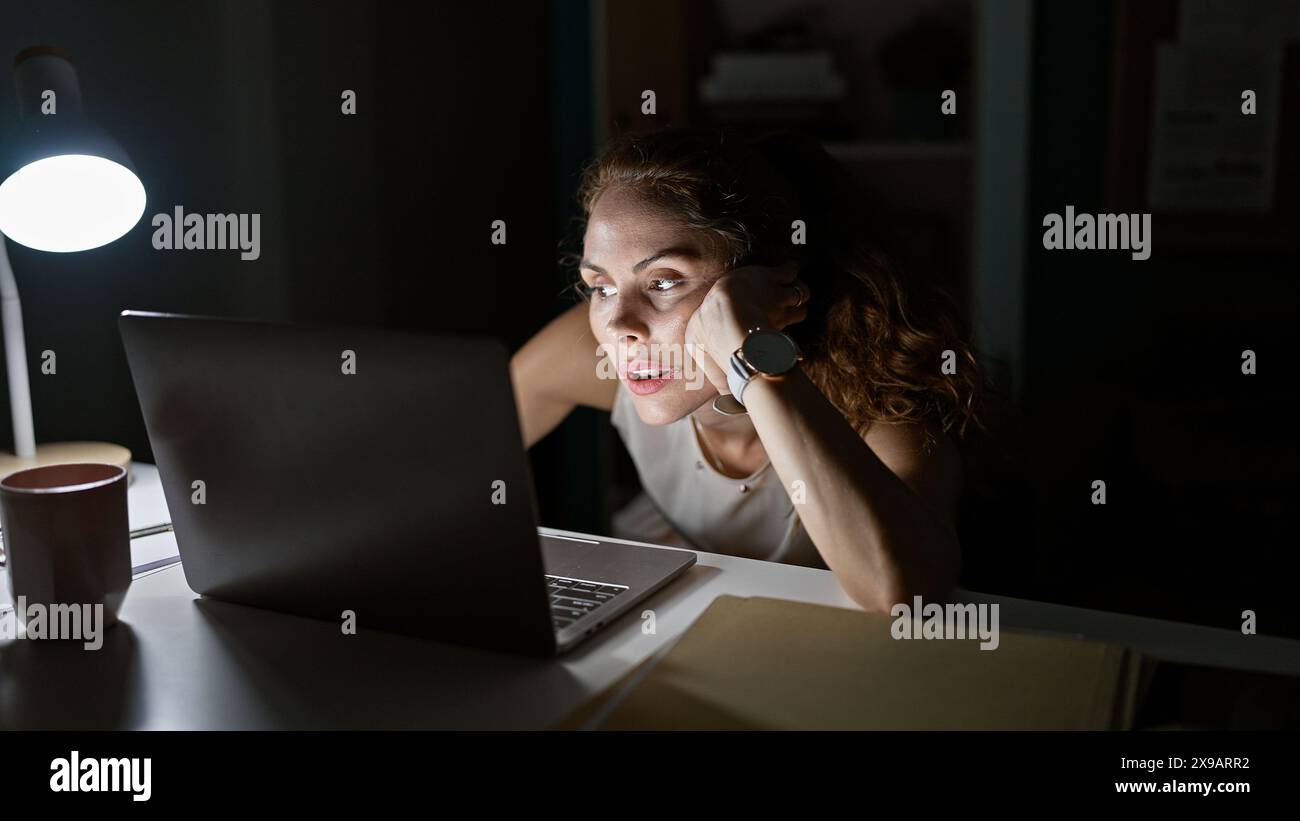 Focused young woman working late at her illuminated office desk ...